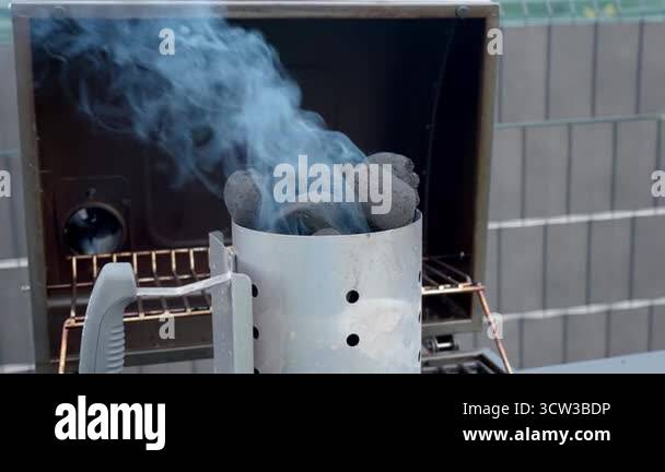Close-up of charcoal chimney starter smoking while heating coals for ...