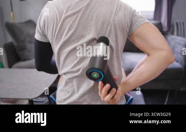 Rear View of Person Using Massage Gun on Back Muscle with Indoor ...