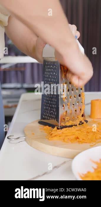 Vertical video. Woman Grating Carrot on Box Grater Over Wooden Round ...