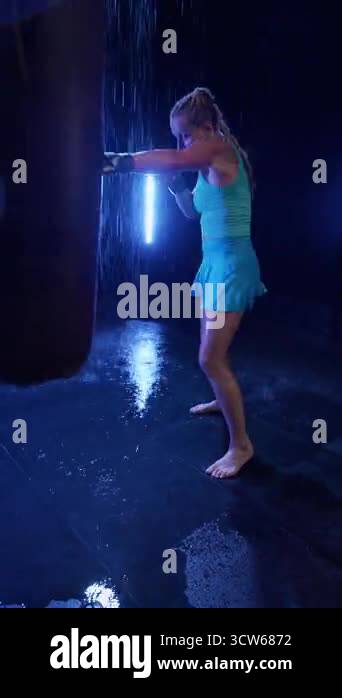 Kickboxing, woman fighter beats a punching bag, training in the dark ...
