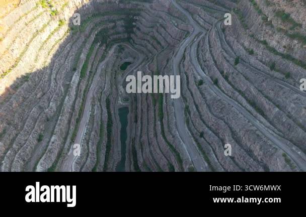 Stone quarry curving downward with tiered walls enclosing emerald pools ...