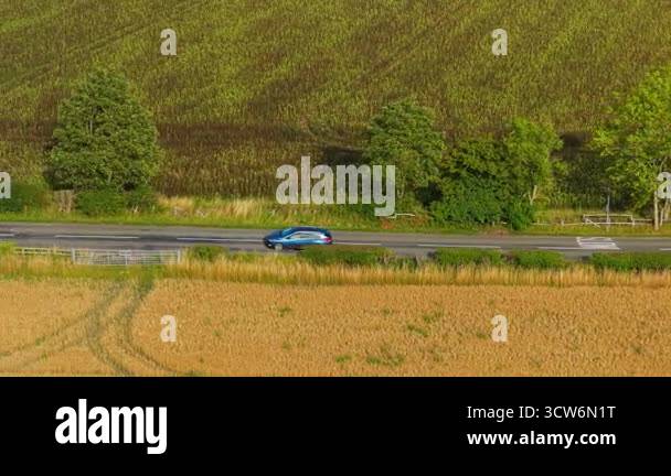 Blue station wagon driving along open countryside road in orange ...