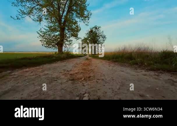 Point of view car driving on dirt road through countryside at sunset ...