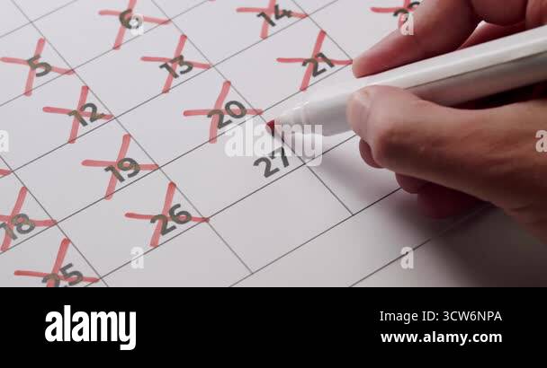 Person using a red marker to cross off dates on a calendar, indicating ...