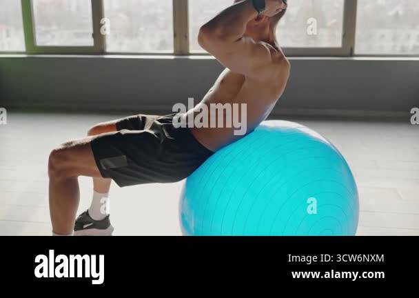 Fit male with toned muscles uses a blue fitness ball for abdominal ...