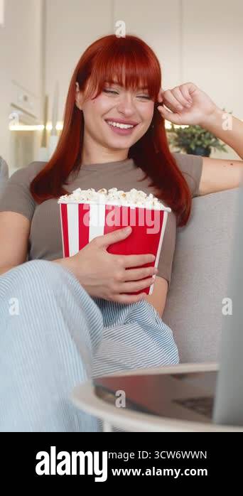 Young woman at home relaxes with popcorn and watches funny movie ...