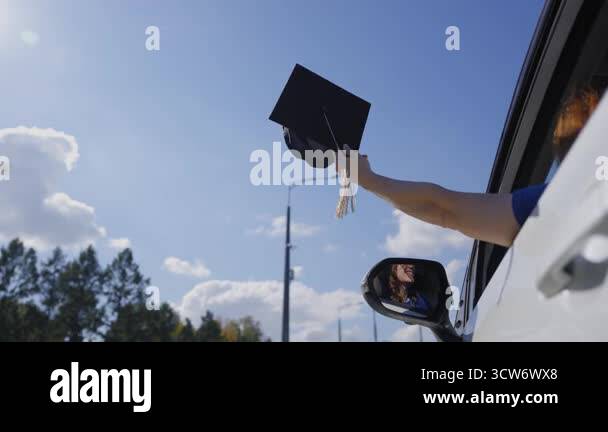 A Caucasian woman waves her graduation cap while extending her arms out ...