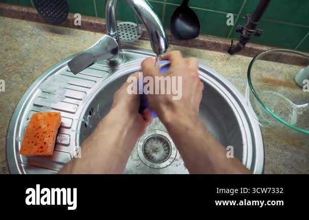 A man washes a blue mug from wash foam in a silver kitchen sink. The ...
