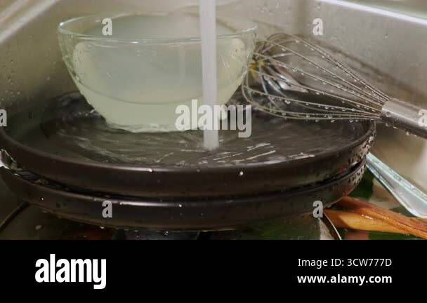 Water flows over a clear bowl and shiny whisk, capturing the essence of ...