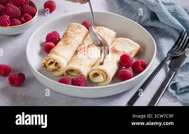 plate of freshly baked rolled crepes decorated with raspberries. cook ...