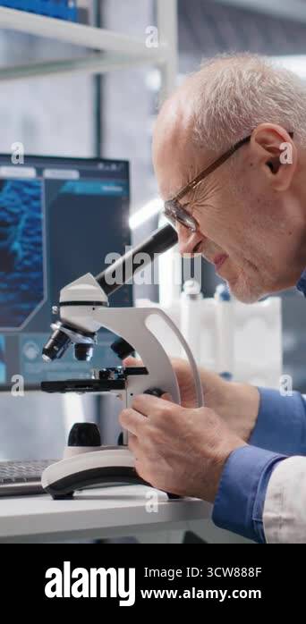 Vertical Video Laboratory with old male scientist observing specimen under microscope. Clinical ...