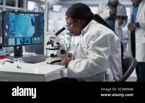 African american scientist placing tray under the microscope, slides ...
