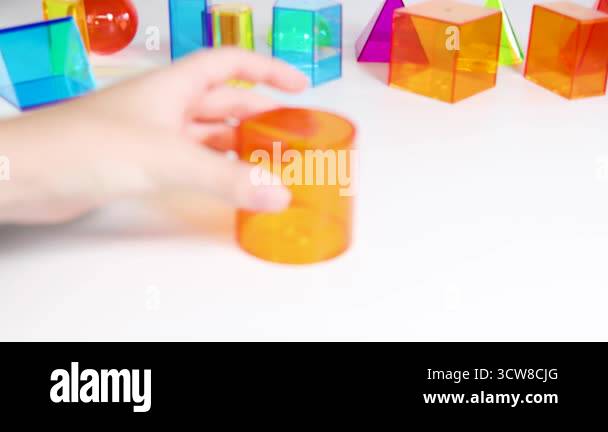 Hands manipulate vibrant 3D geometric shapes on a white surface ...