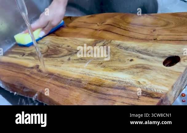 A person scrubs a large wooden cutting board with a sponge under a ...