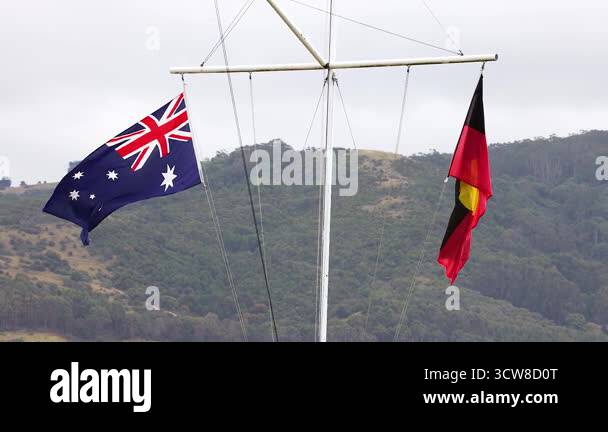 Australian and Aboriginal flags flutter against a hilly backdrop ...