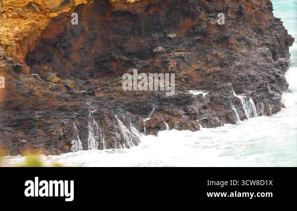 Dynamic waves crash against rugged cliffs under natural light, showcasing the dramatic coastal ...