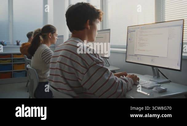 Male Student Learning Programming at Computer in Bright Classroom. Group Young People in IT ...