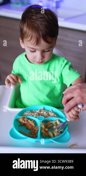 Cute toddler takes food from the plate. Mom's hand supports the kid's ...