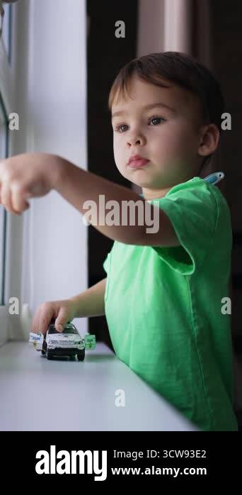 Serious Caucasian kid stand at the window pointing at glass with his ...