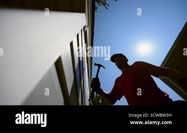 Worker hummers a nail into plastic panel siding on outside wall of the ...
