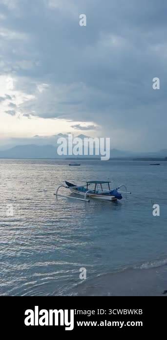 Traditional outrigger boat floating on gentle waves with distant ...