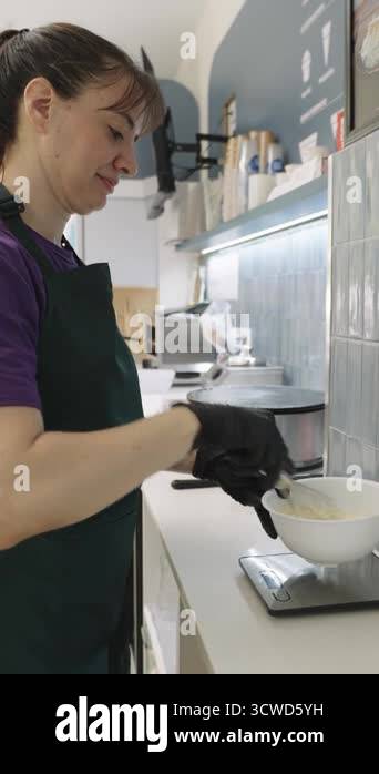 Professional pastry chef in an apron and gloves carefully weighing ...