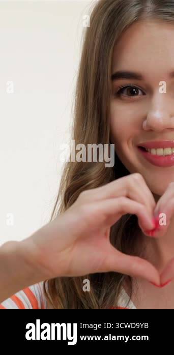 A radiant brunette woman joyfully forms a heart shape with her hands ...
