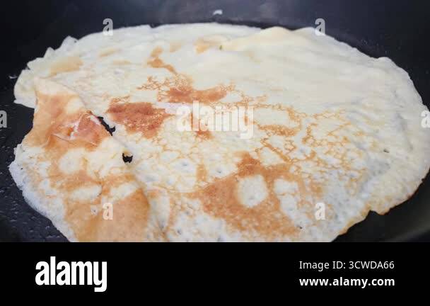 A close-up view of a homemade crepe cooking in a frying pan. the crepes ...