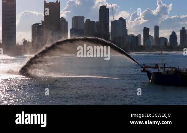 A dredging ship pumps sand onto a beach against a city skyline, under ...