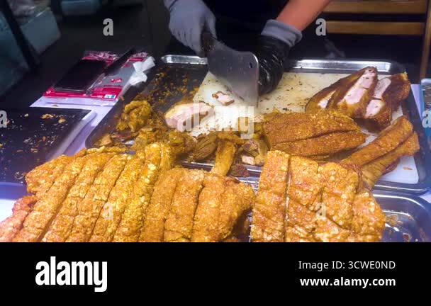 A vendor slices crispy pork at a bustling Bangkok market. Bright ...