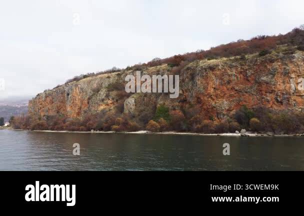 Rocky cliff face on the shoreline with a thin layer of trees and ...