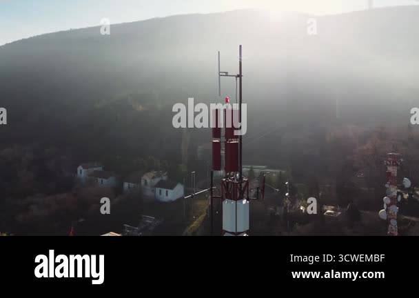 Telecommunication tower with a red light in a misty morning with bright ...