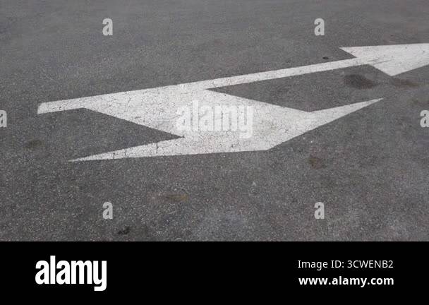White arrow painted on asphalt road surface. Video shows a weathered ...