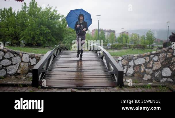 Captured moment of a young woman walking joyfully with a blue umbrella ...