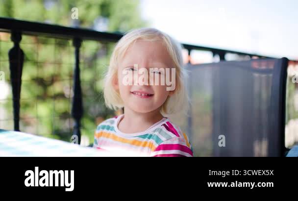 A happy little girl with blonde hair enjoys a tasty snack at a table on ...