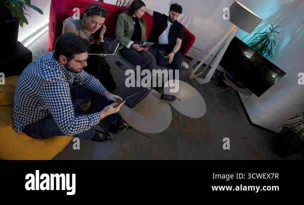 Four colleagues sit together using electronic devices, including phones ...