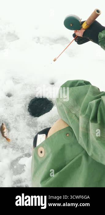 Winter fishing. Fisherman is catching fish with fishing rod in ice hole ...
