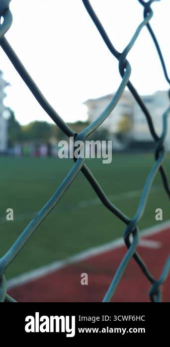 Mesh fence, close up. Unfocused football field behind mesh fence. View ...