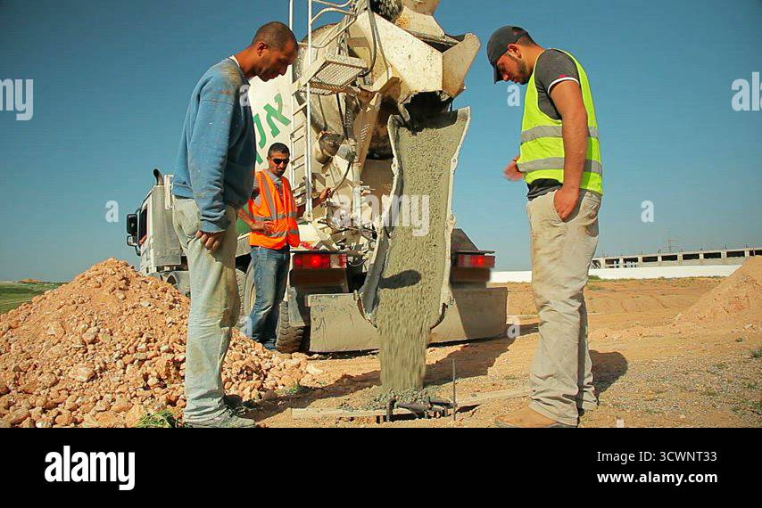 Construction workers pouring concrete in to a hole in the ground from ...