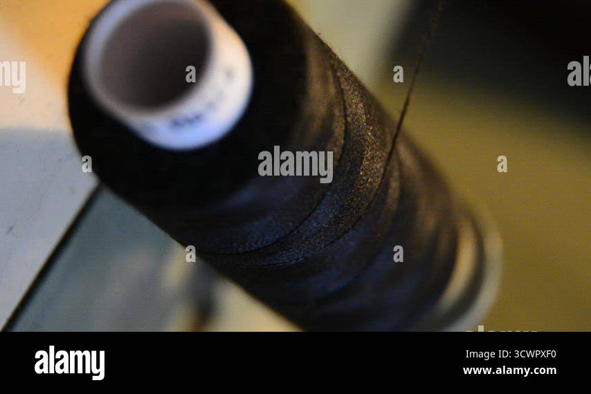 spool of black thread with needle stuck. Unrolls during process of ...
