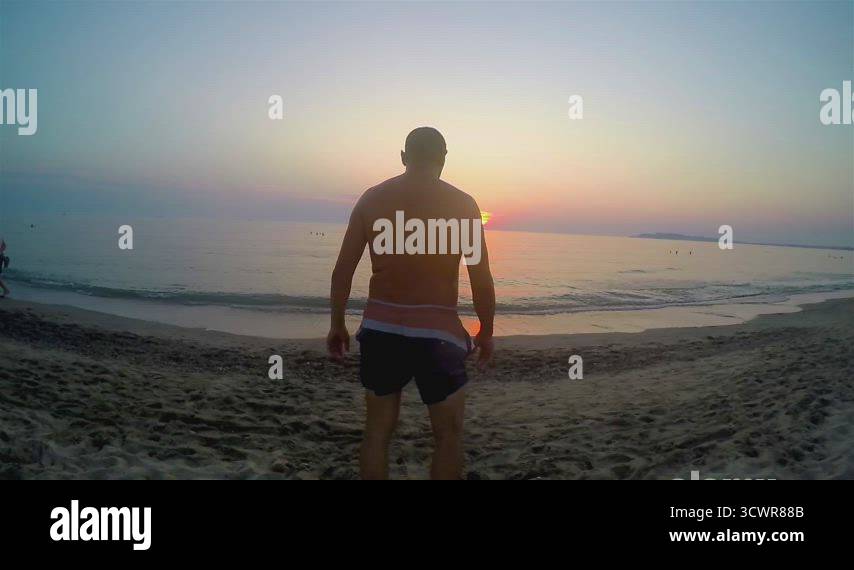 happy man running on the beach against sunset reflection and jumps in ...