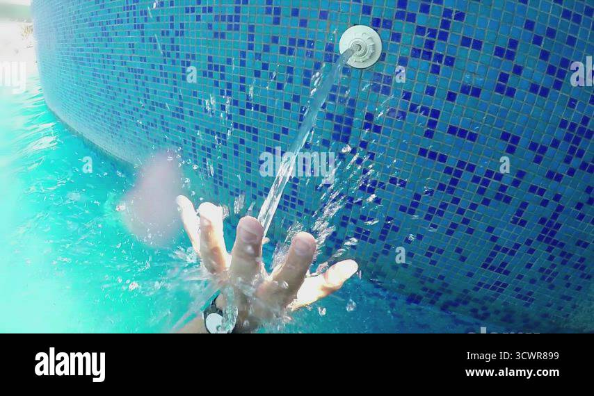 Hand playing with the clear water jet drops jumping in the air from a ...