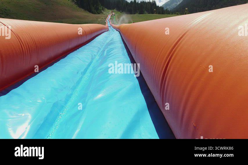 Girl Sliding down the 300 meters long water slide on mountain meadow ...