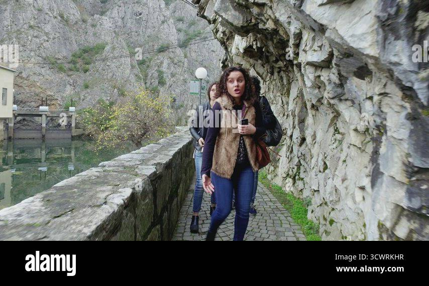 Three female tourists walking on narrow walkway path carved on rocky ...