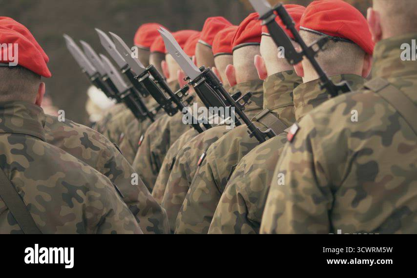 Soldiers in red berets with guns stand with their backs to the camera ...