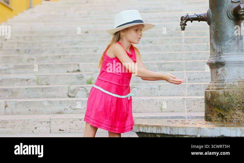 Little adorable girl drinking water from the tap outside at hot summer ...
