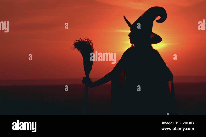 side view girl in fancy dress witch holds a broom looking on sunrise ...