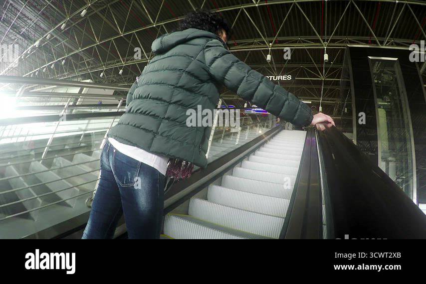 Attractive female on airport departure escalator wave hand farewell ...