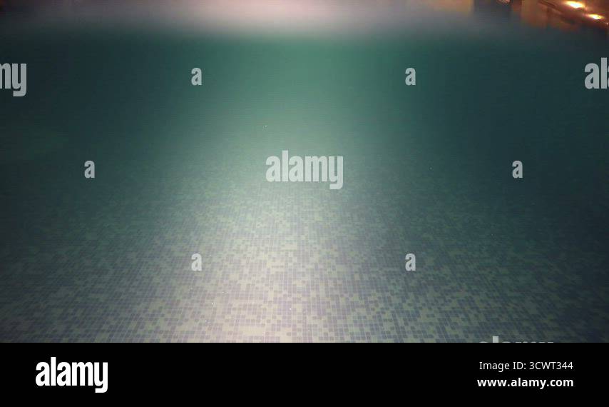 Pool surface in dark atmosphere at night, hotel spa complex. View ...