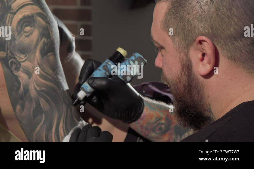 Rear view shot of a tattoist making tattoos on the arm of male client ...